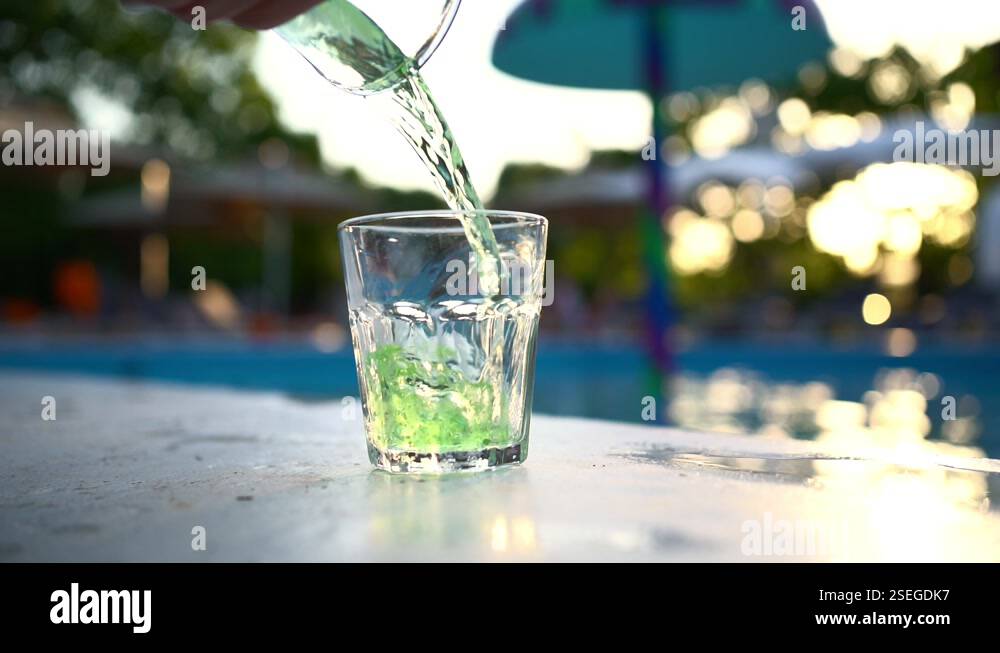 Green refreshing drink is poured from bottle into glass backdrop swimming pool Stock Video ...