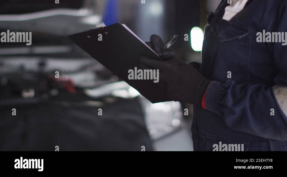 Mid section of female mechanic taking notes on clipboard at a car ...