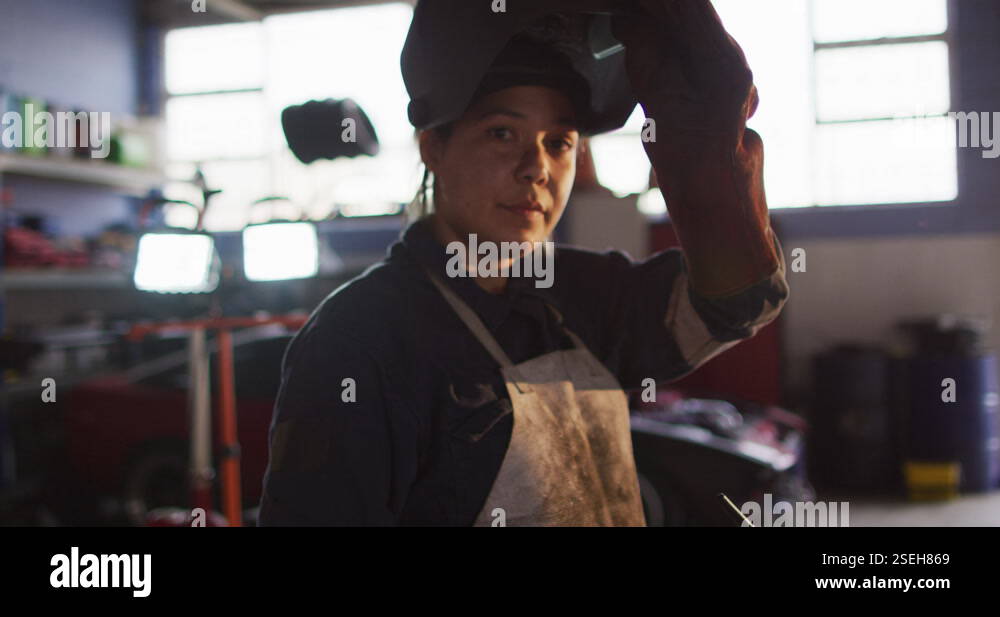 Portrait of female mechanic removing welding helmet at a car service ...