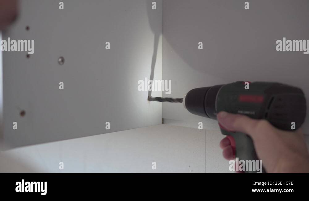 Furniture maker drills holes with a drill in side of the kitchen module ...