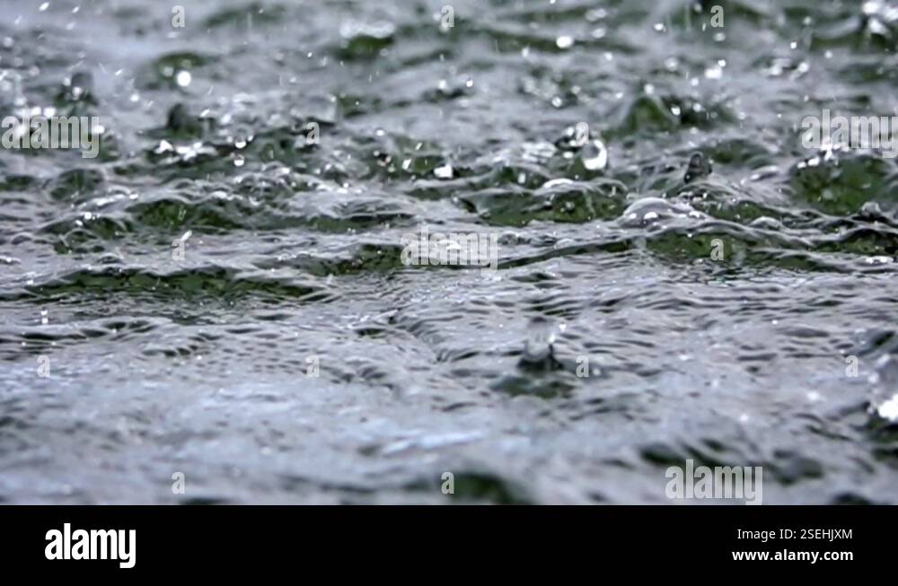 Close-up of rain falling on water surface, splashing water drops around ...