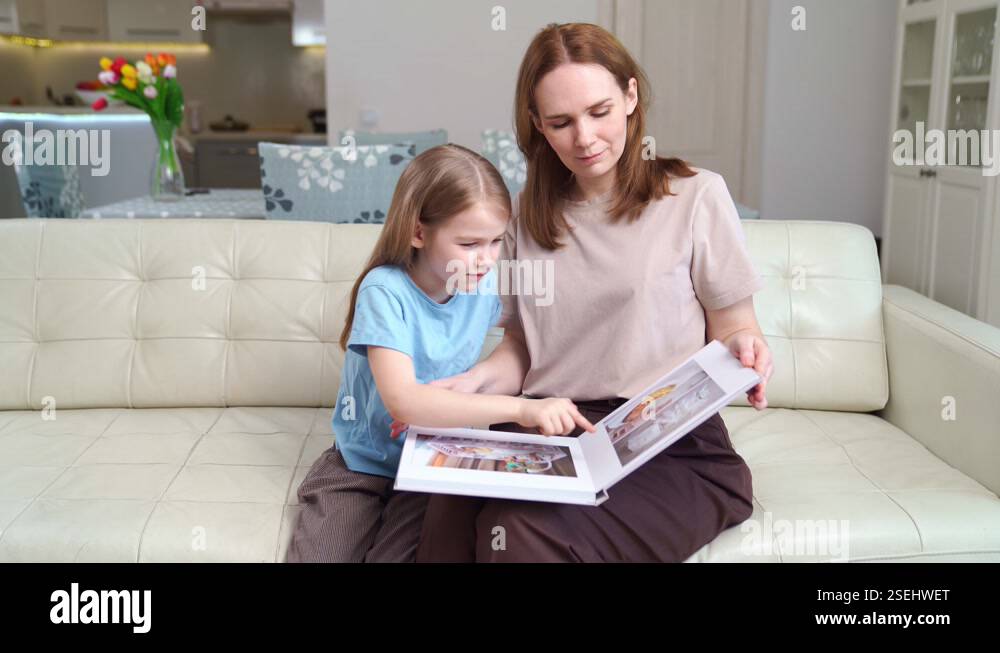 mother and daughter looking a book with photos from a family photo ...