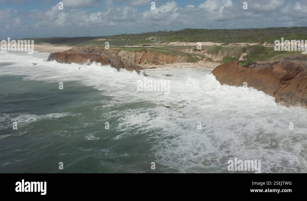 Aerial of a wild sea slamming into cliffs and flowing into a small bay ...