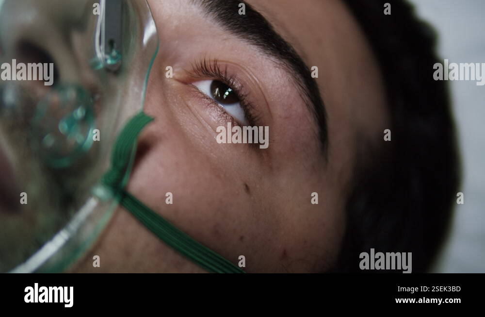 Patient with oxygen mask opening eyes after operation, lying in ...