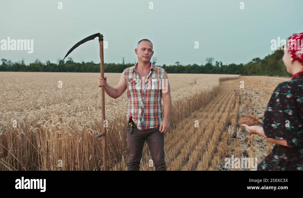 A farmer with a scythe and a girl with bread stand in the field, a ...