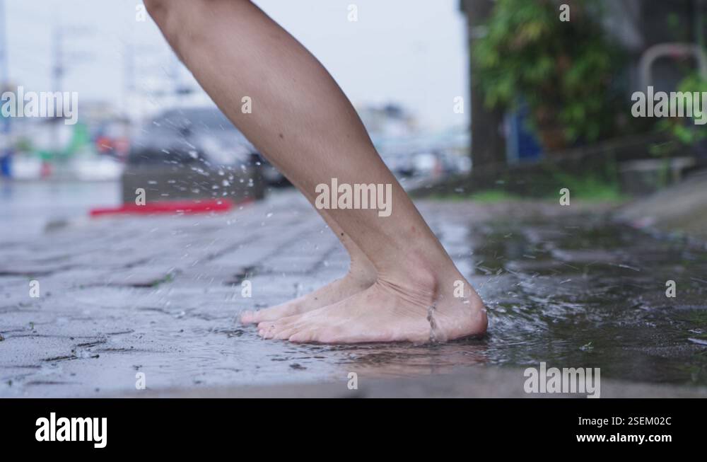 Close up light skin asian girl barefoot stomp and playing on puddles ...