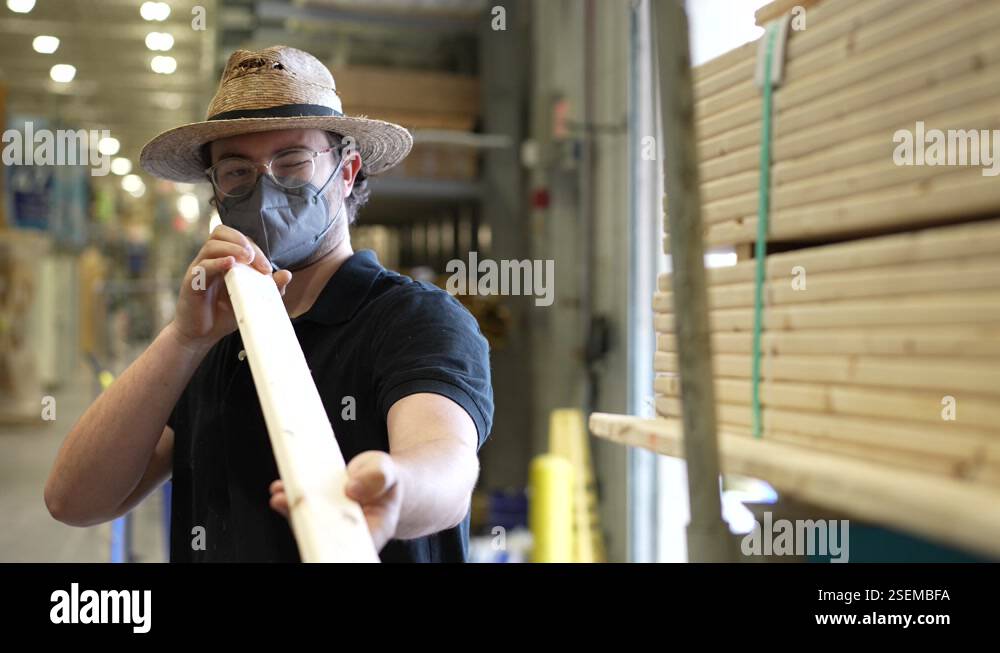 A man wearing a face masks sights down a length of lumber checking to ...