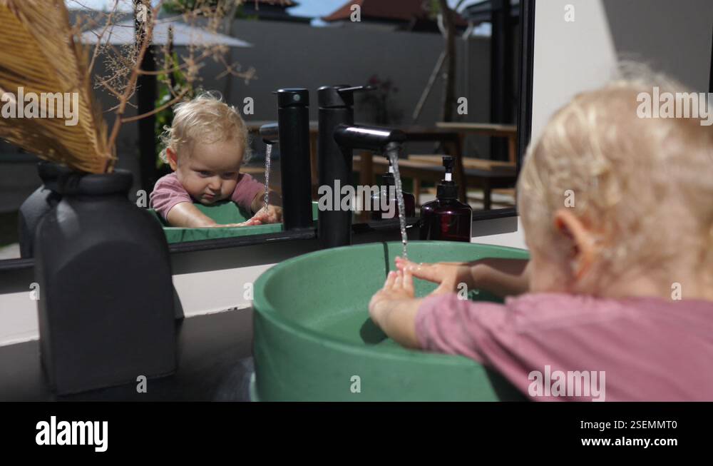 Caucasian toddler baby playing with the running tap water by the green ...