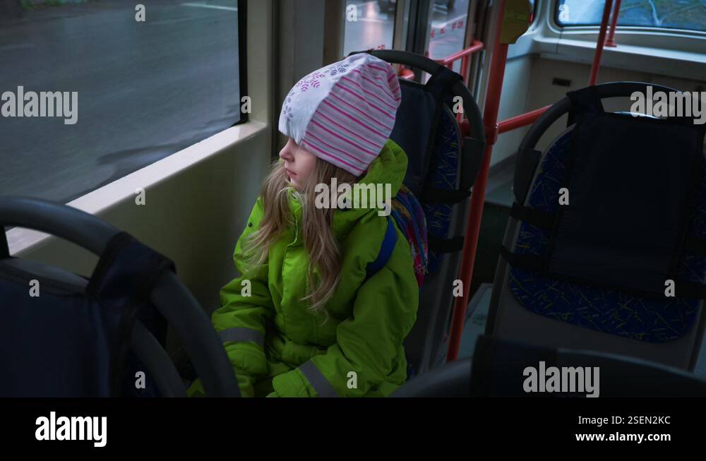 Blonde child watches road from window while sitting in moving tram in ...