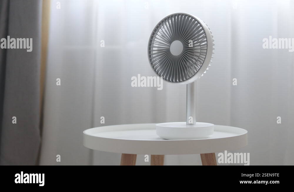 White desktop electric fan on light wooden table. Turning on the fan ...
