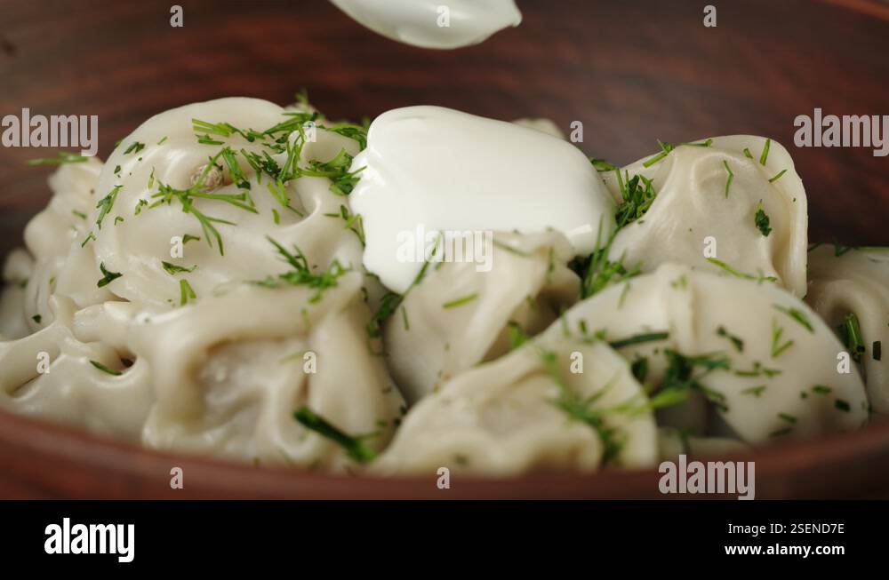 Adding sour cream into boiled dumplings on board close-up, cooking ...