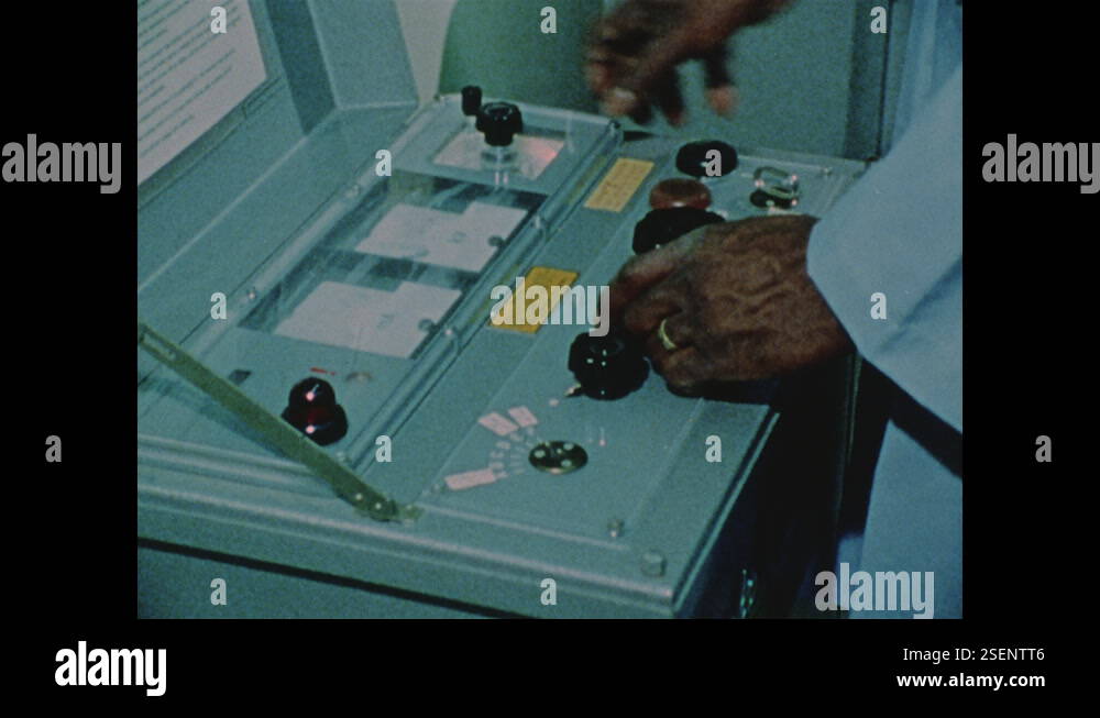 1960s: Lab worker uses machinery in x-ray lab. Red light flashes ...