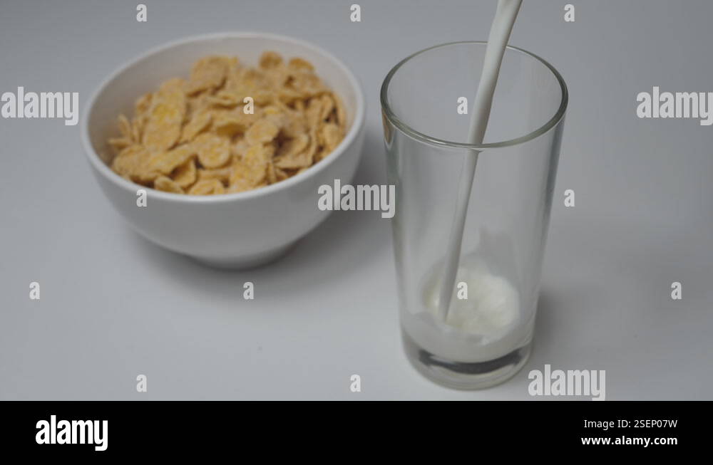 Pouring milk into a glass beaker on a white table. Healthy breakfast ...