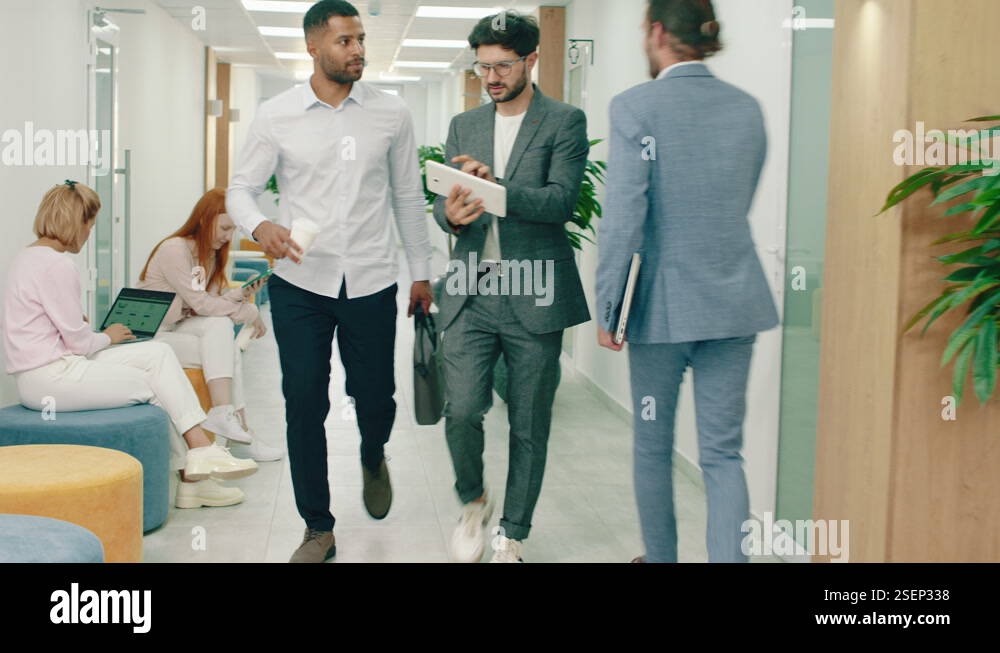 Two work colleagues are walking and talking through the office passing ...