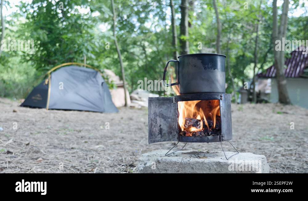 Blackened with soot pot boiling over burning fire wood stove on tourist ...