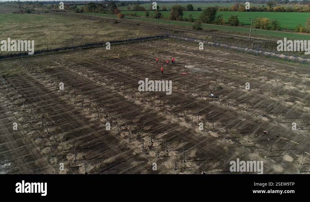 Field with workers and lots of poles in ground for solar panel mounting ...