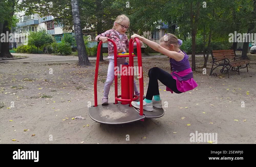 Two girls spinning on a carousel in a playground. Children having fun ...