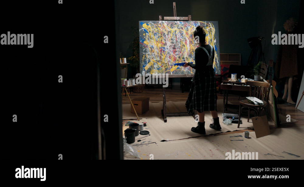 Hidden shot from behind easel dark studio lit by lamp at night artist ...