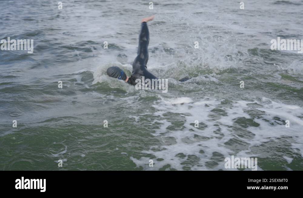 Hardy triathlete in a wetsuit swims in open water, an athlete trains ...