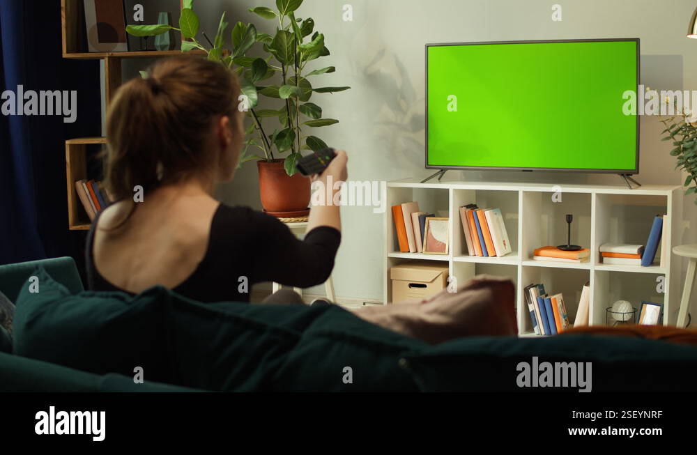 Woman watching TV with green screen in living room back view. Female ...