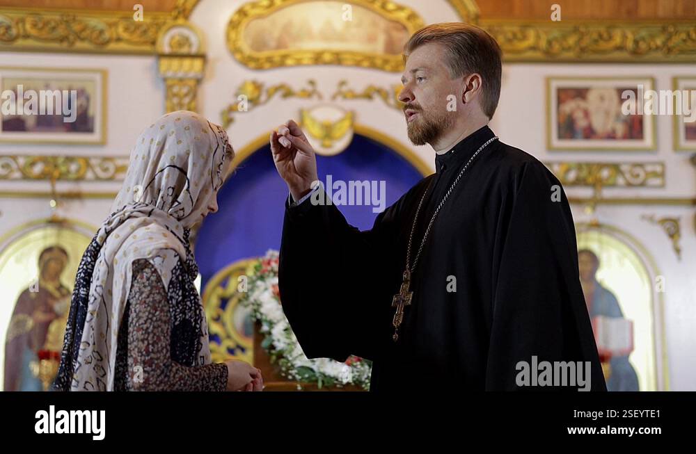 a priest blesses a teenage girl in a headscarf in an Orthodox church ...