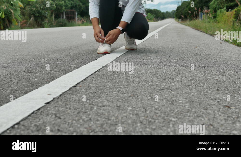 Female runner stops tying her shoelaces while jogging on road trail in ...