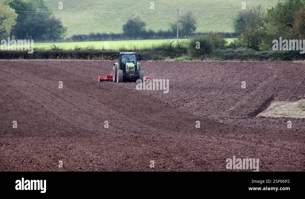A farmer driving a tractor tilling and raking a ploughed field during ...