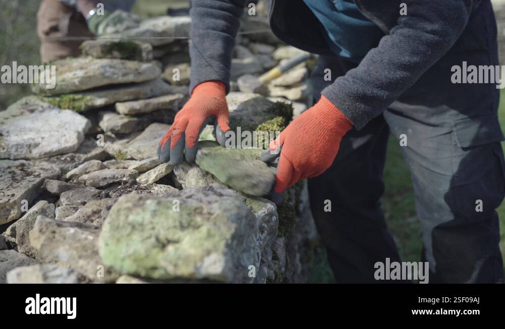 Man hands only building dry stone wall, placing stones to make wall ...