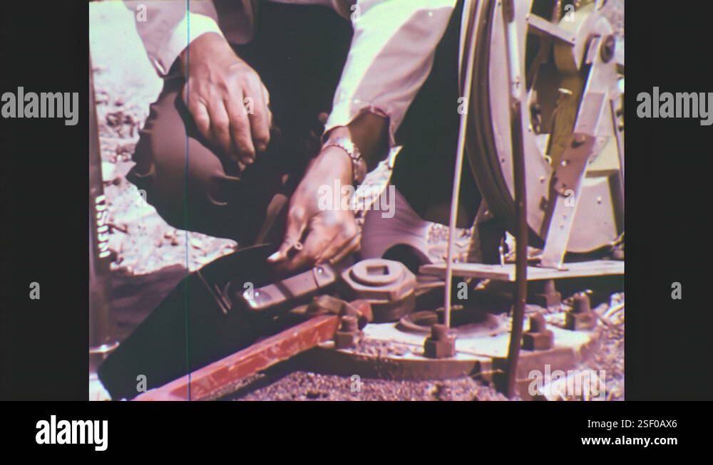 1970s: Man in helmet kneels over tools, screws canister. Bolted pipe ...