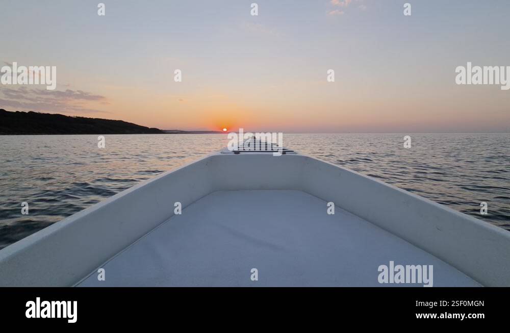 Bow of boat moving forward over sea water pointing toward golden sunset ...
