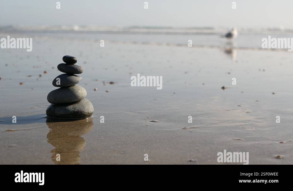 Rock balancing on ocean beach, stones stacking by sea water waves ...