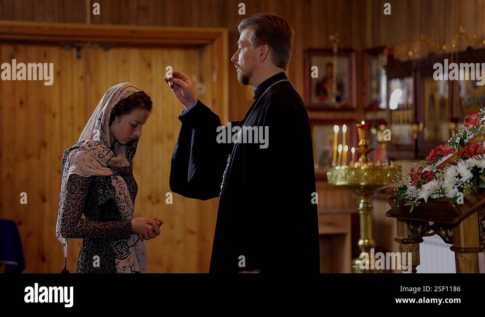 a priest blesses a teenage girl in a headscarf in an Orthodox church ...