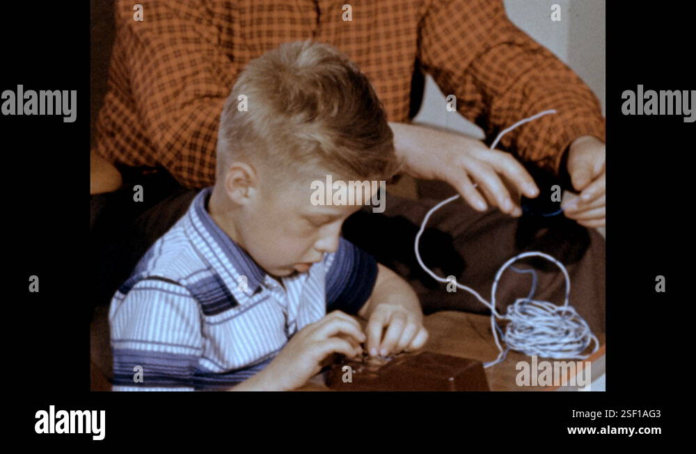 1950s: Slate. Man uncoils spool of wire while a boy struggles with a ...