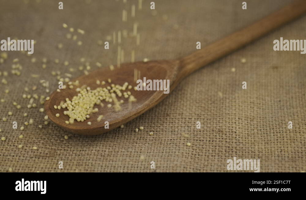 Slow motion. Millet seeds falling into a wooden spoon lying on a burlap ...