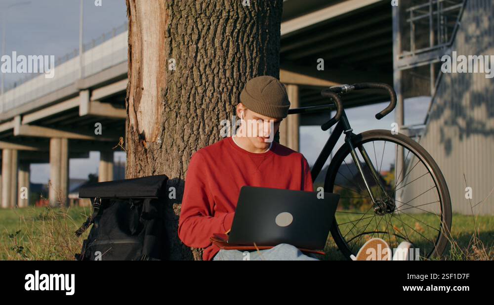 A man uses a graphics tablet and a laptop, sitting on the ground under ...