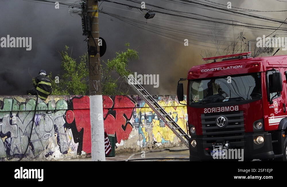 Fireman suppresses large smoky urban fire from atop concrete wall, on ...