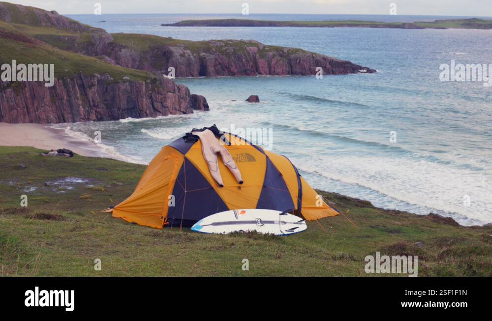 Surfer camping in a tent on the top of the cliff overlooking a cold and ...