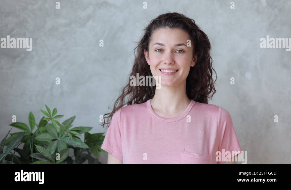 Attractive woman portrait looking into camera by grey wall 4k video ...