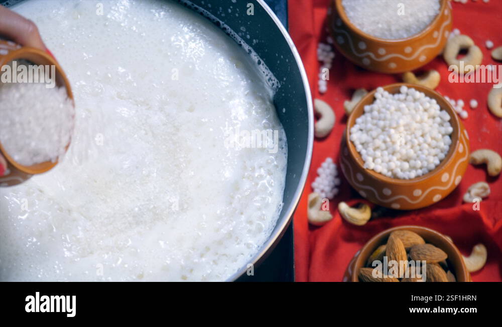 An Indian cook adding sugar into the milk mixed with white tapioca ...