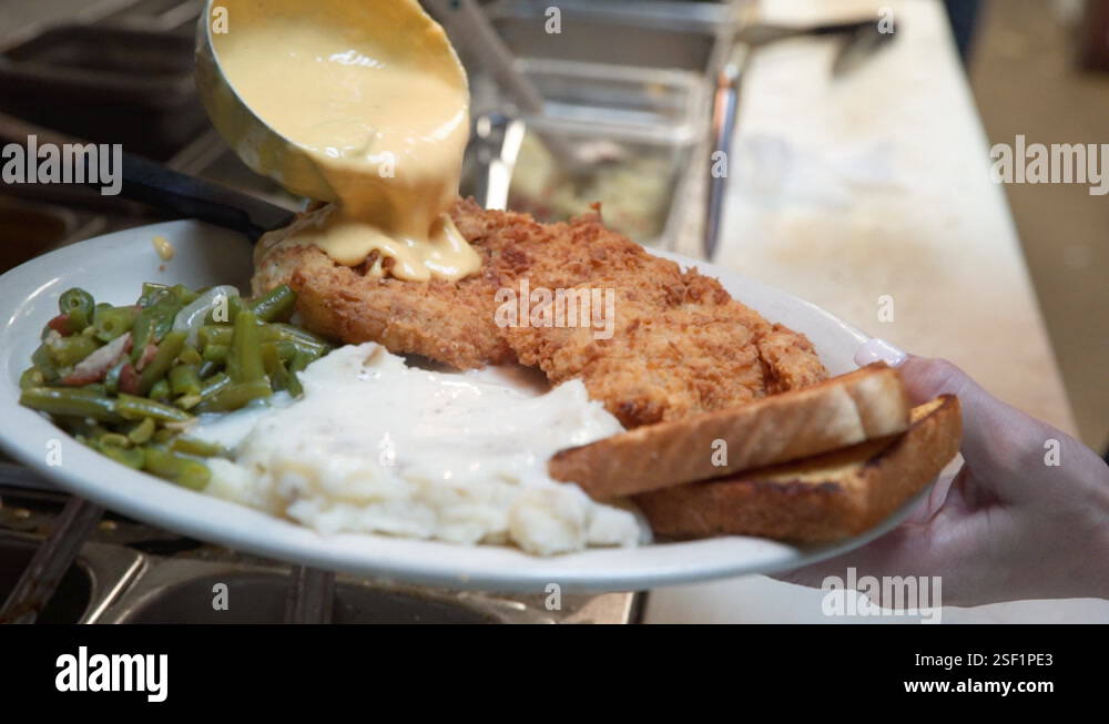 Cook pours queso over chicken fried steak, ladle layers cheese sauce ...