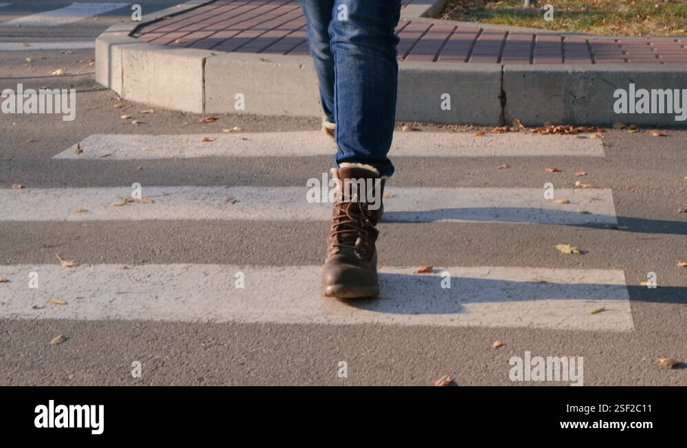 A woman in brown shoes crosses the road at a pedestrian crossing, legs ...