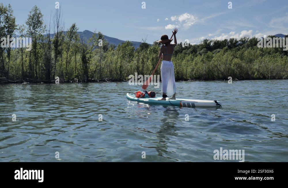 Young sportive woman on a stand up paddle board rowing on calm lake ...