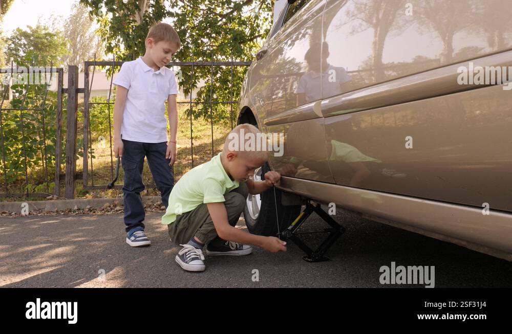 Two curious little boys help Dad fix the car, they lift the car with a ...