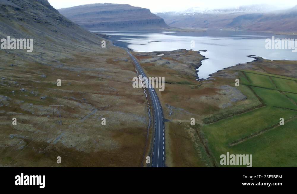 A drone tracking lone white car driving along the road with black sand ...