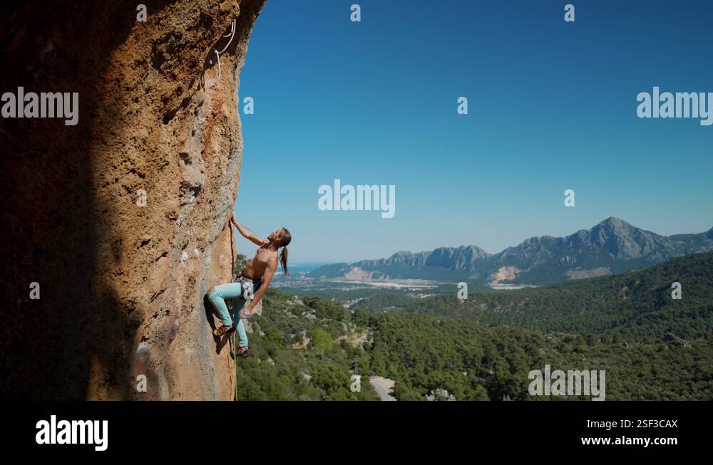 muscular man rock climber in bright blue pants climbing the challenging ...