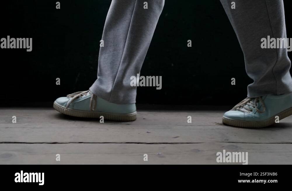 feet in blue sneakers and gray pants walk on unpainted boards against a ...