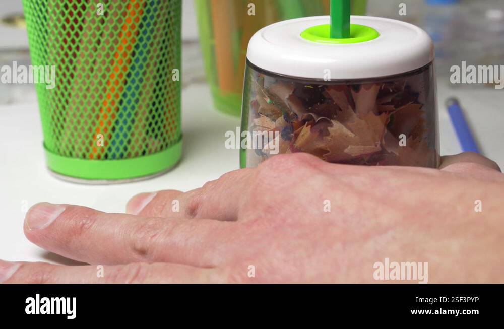 A man sharpens a pencil with an electric sharpener with shavings inside ...