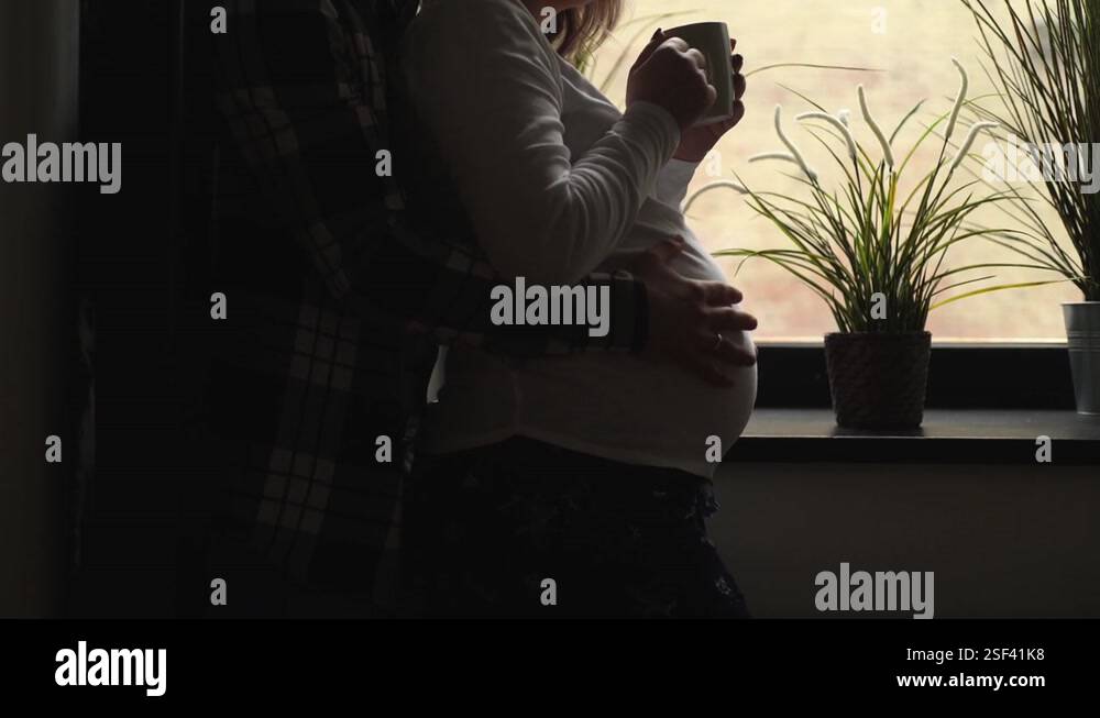 man hugs pregnant wife with large tummy and cup near window Stock Video ...