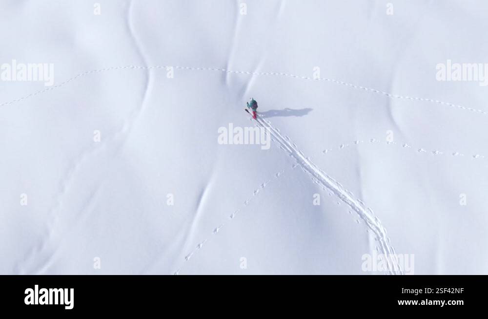 TOP DOWN: Flying above a split boarder trekking uphill on a sunny ...