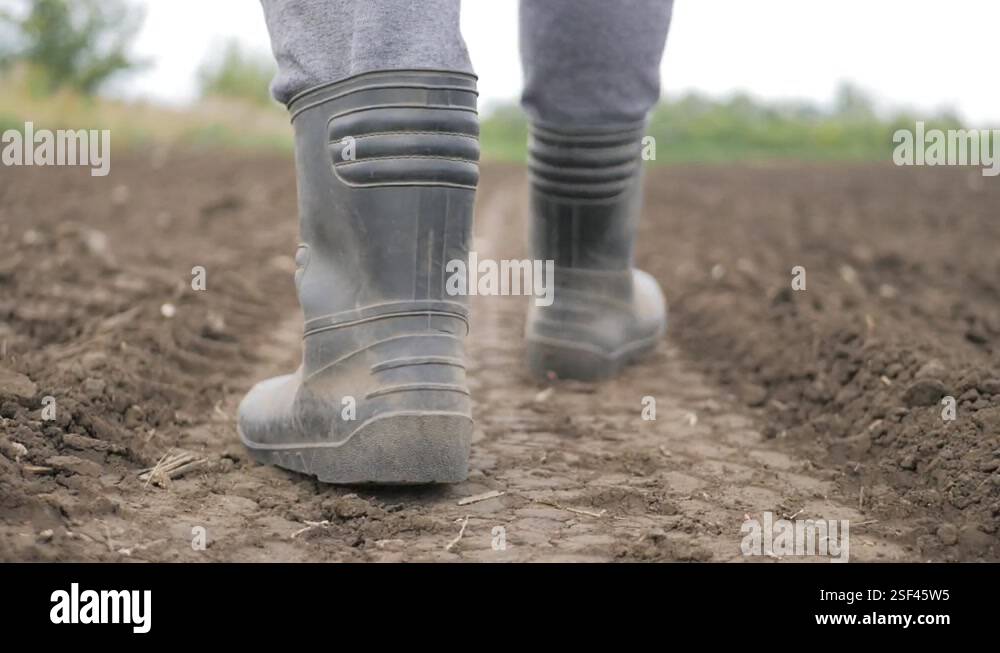 Farmer goes with rubber boots along plowed field. Rubber boots for work ...